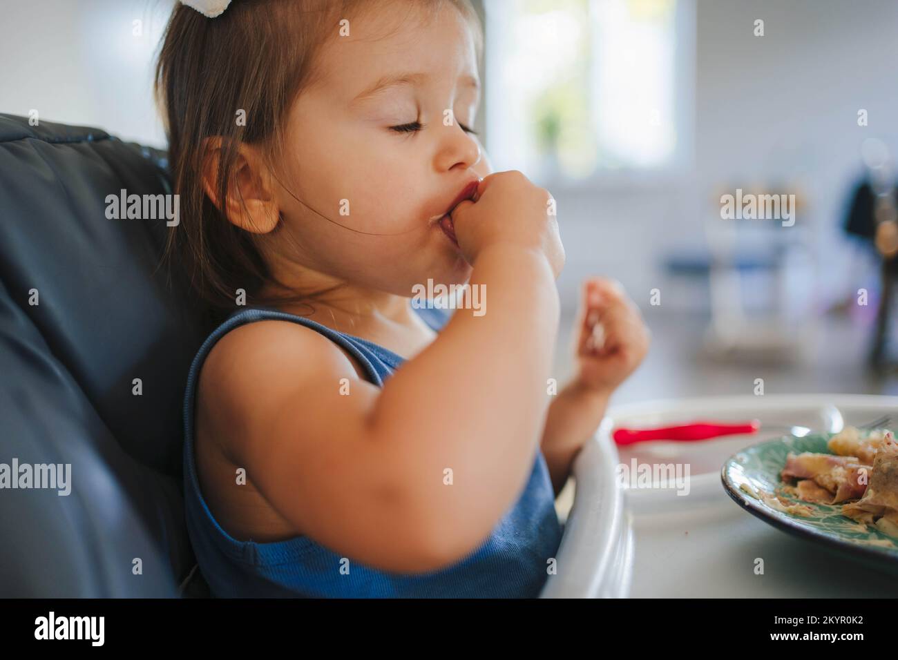 Headshot portrait of cute baby girl eating on high chair, self-feeding ...