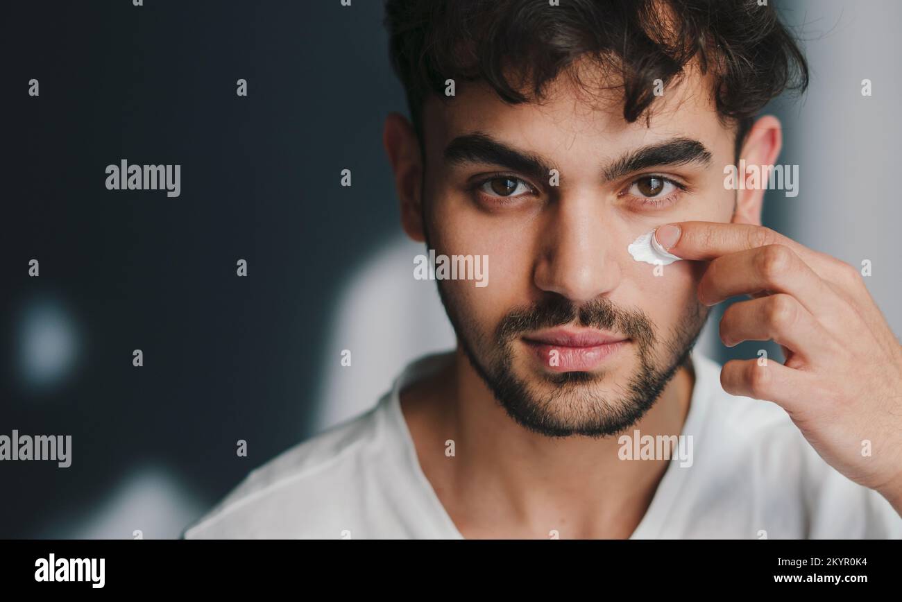 Head Shot Of Handsome Young Man Applying Anti Aging Moisturiser On Face