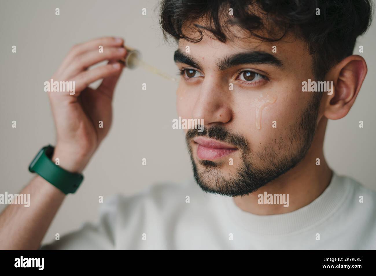 Close-up portrait of young handsome man applying serum product on his ...