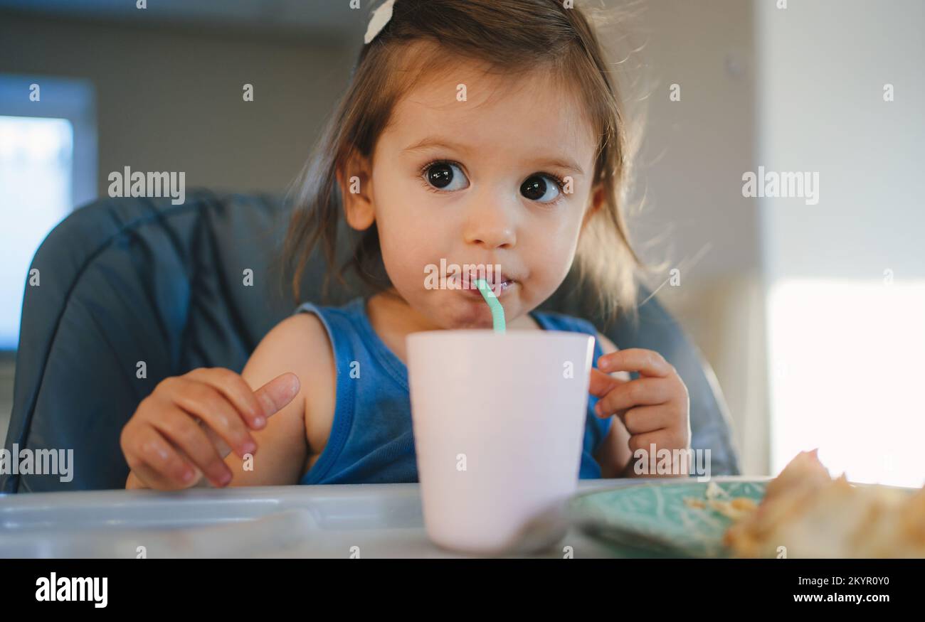 Baby girl sitting on the chair and drinking water from the glass with a ...