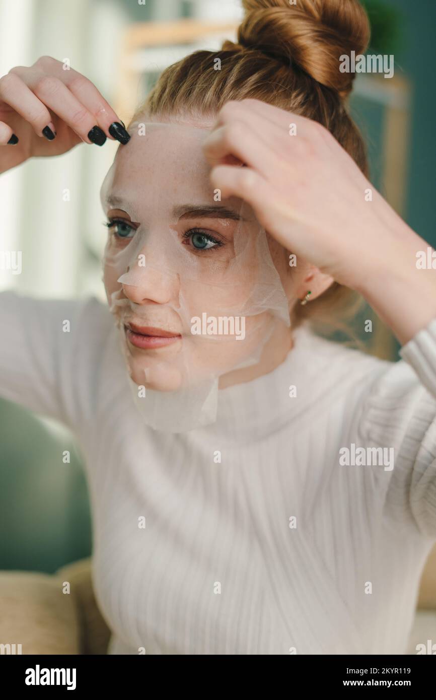 Beautiful young caucasian red-headed woman with paper sheet mask ...