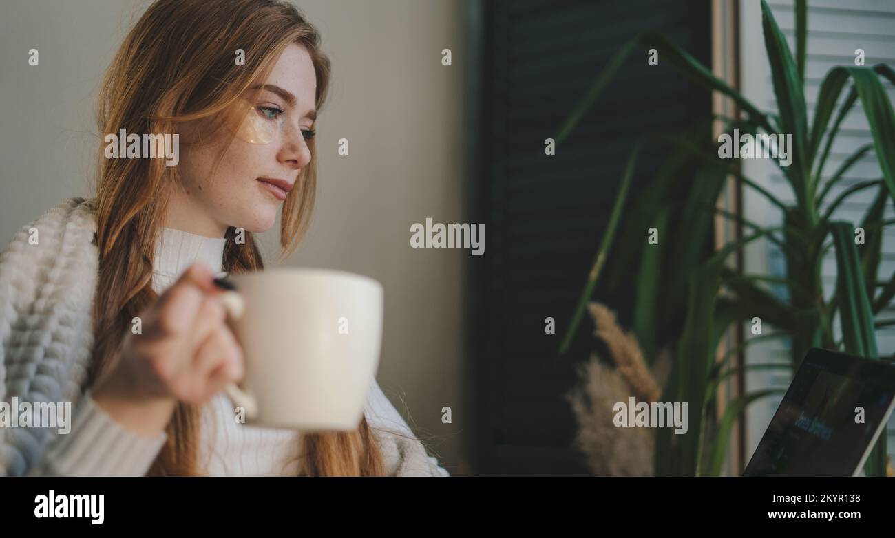 Happy young ginger woman with eye-patches under eyes drinking coffee ...