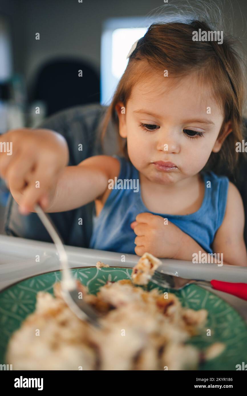 Portrait of happy young baby girl sitting on high chair and feed her ...