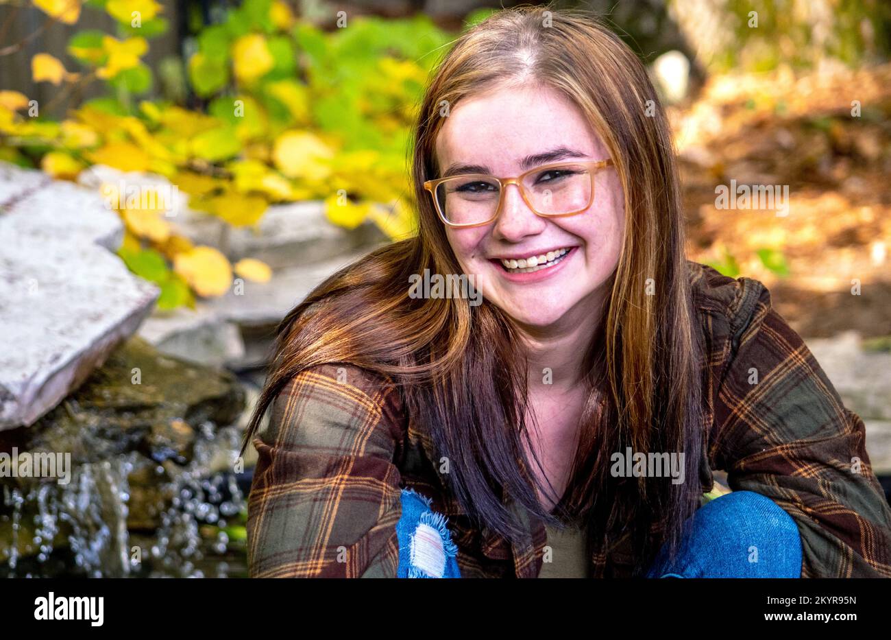 Happy girl poses for a senior photo in a flannel shirt and torn jeans ...