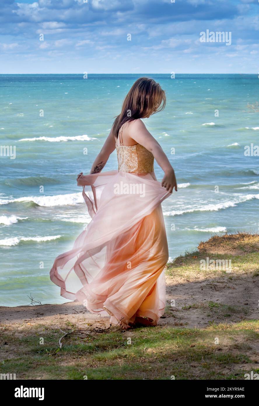 pretty young girl in a flowing pink dress, walks along a ledge high ...