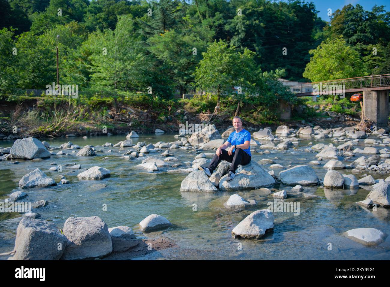 A man in blue clothes sits on a rock by the river Stock Photo - Alamy