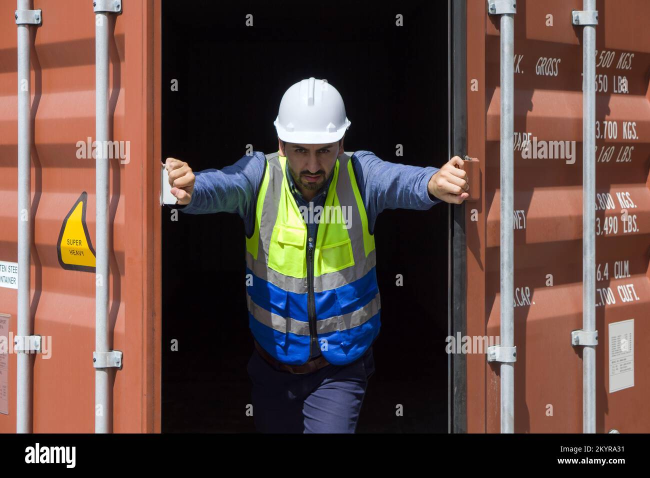 Young worker with safety vest and yellow hardhat pushing container door ...