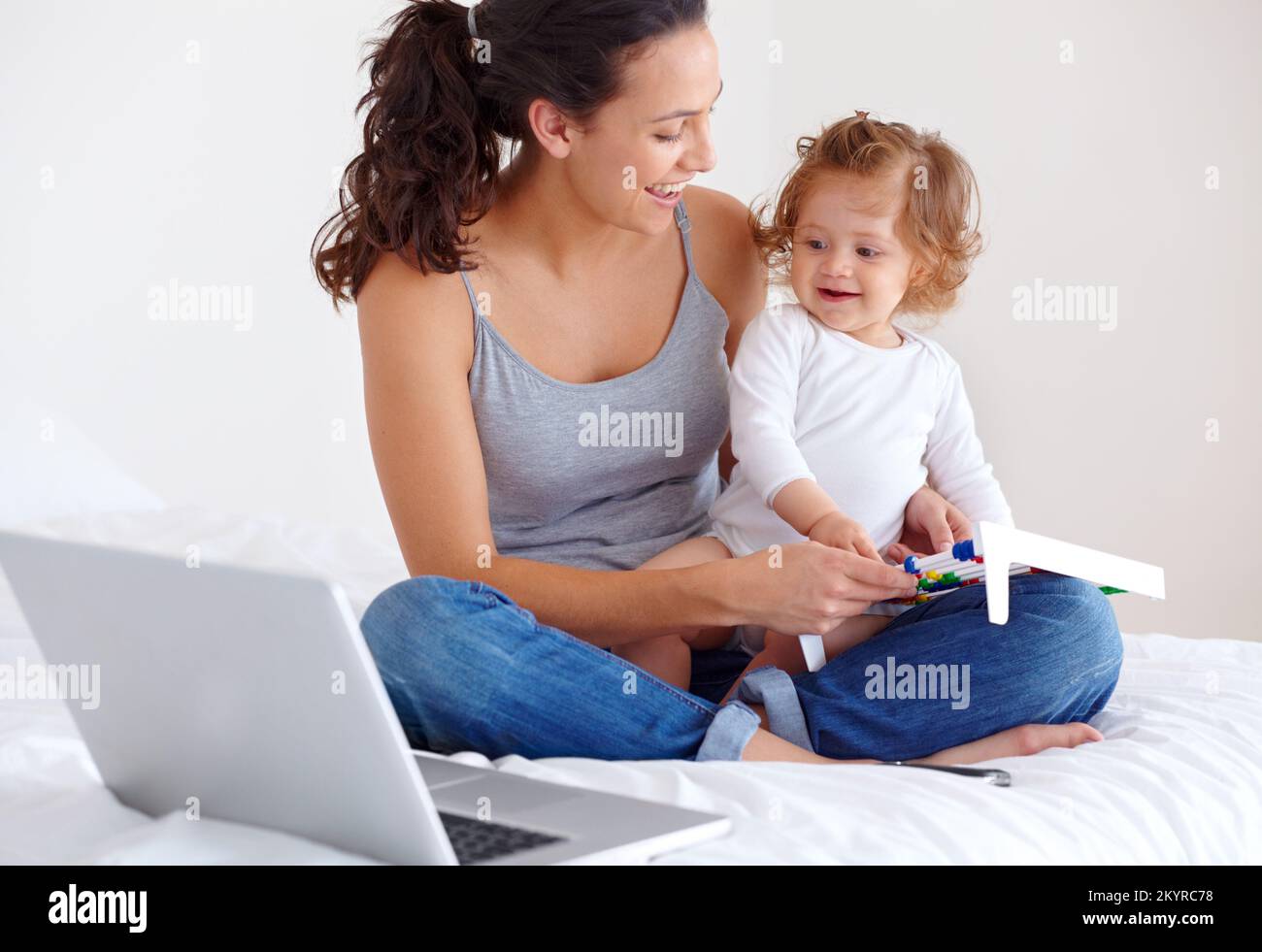Juggling motherhood with work. A young mother sitting on a bed with her ...