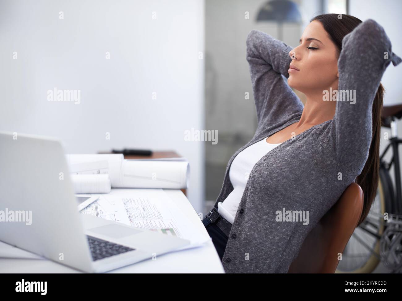 Taking a quick breather. an attractive designer leaning back in her chair with her hands behind ...