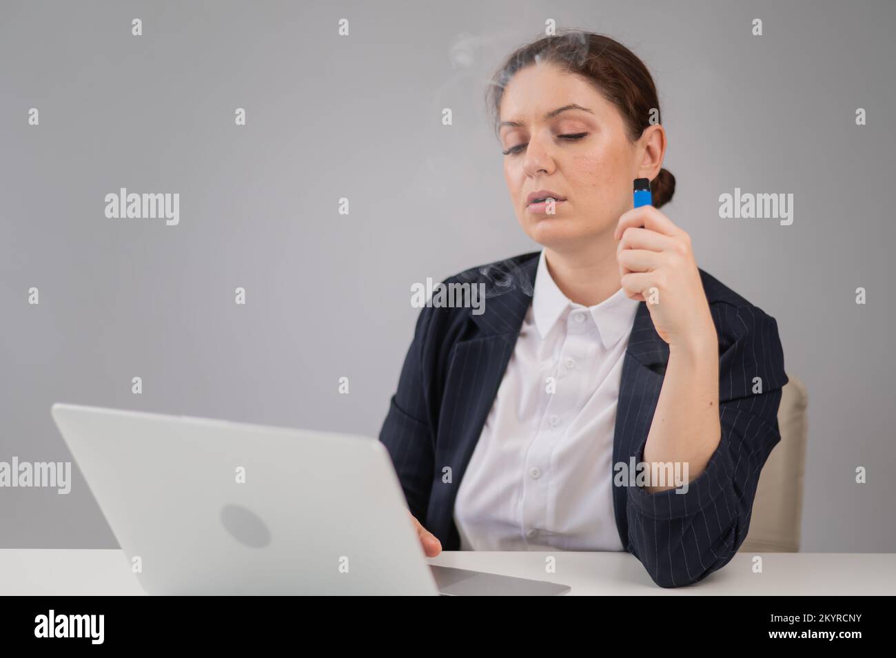 Business woman smoking a disposable vape while sitting at her desk ...