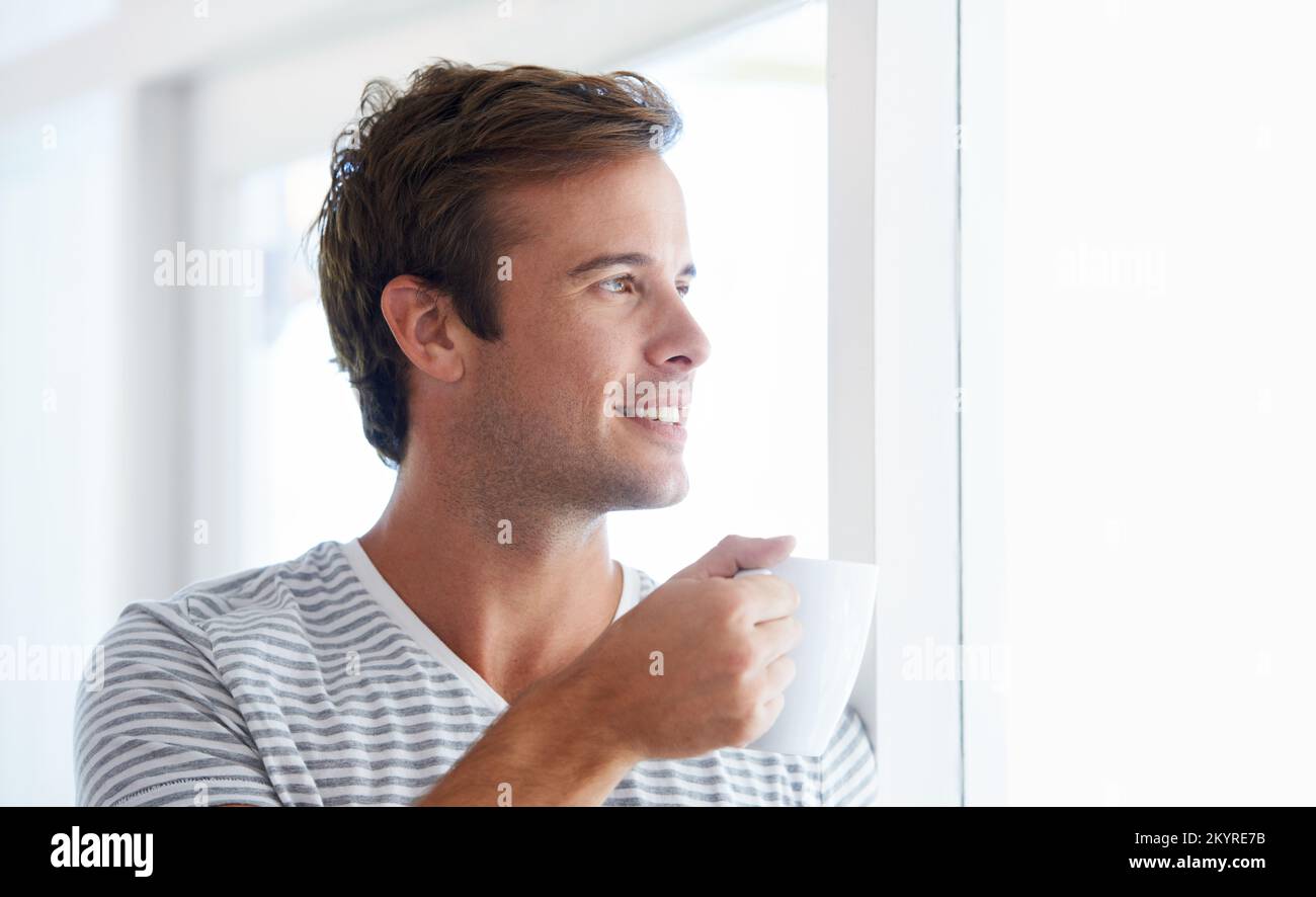 Thinking about the day ahead. A young man smiling while drinking a cup ...
