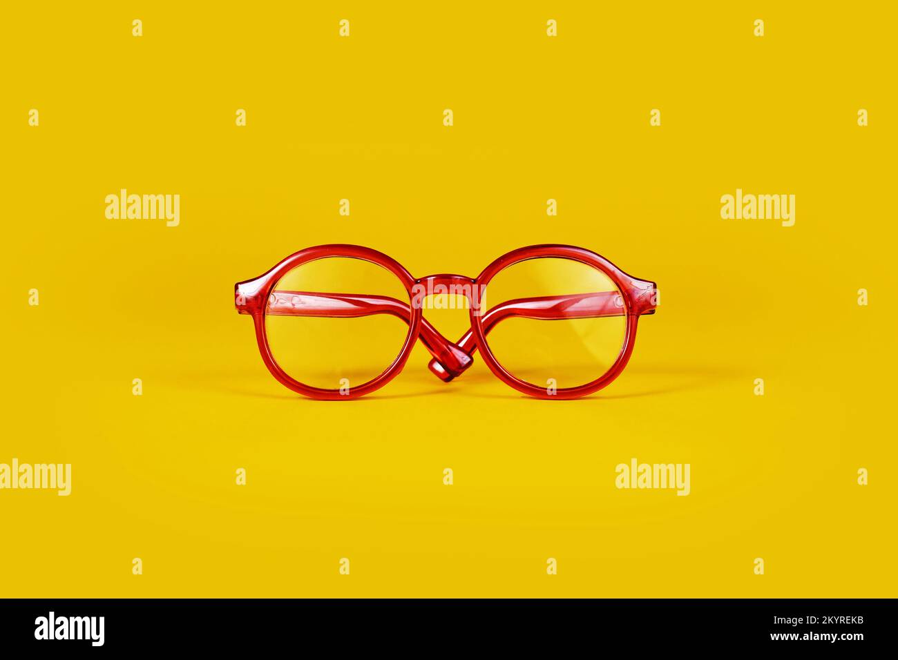 Small red round eye glasses on yellow background Stock Photo - Alamy