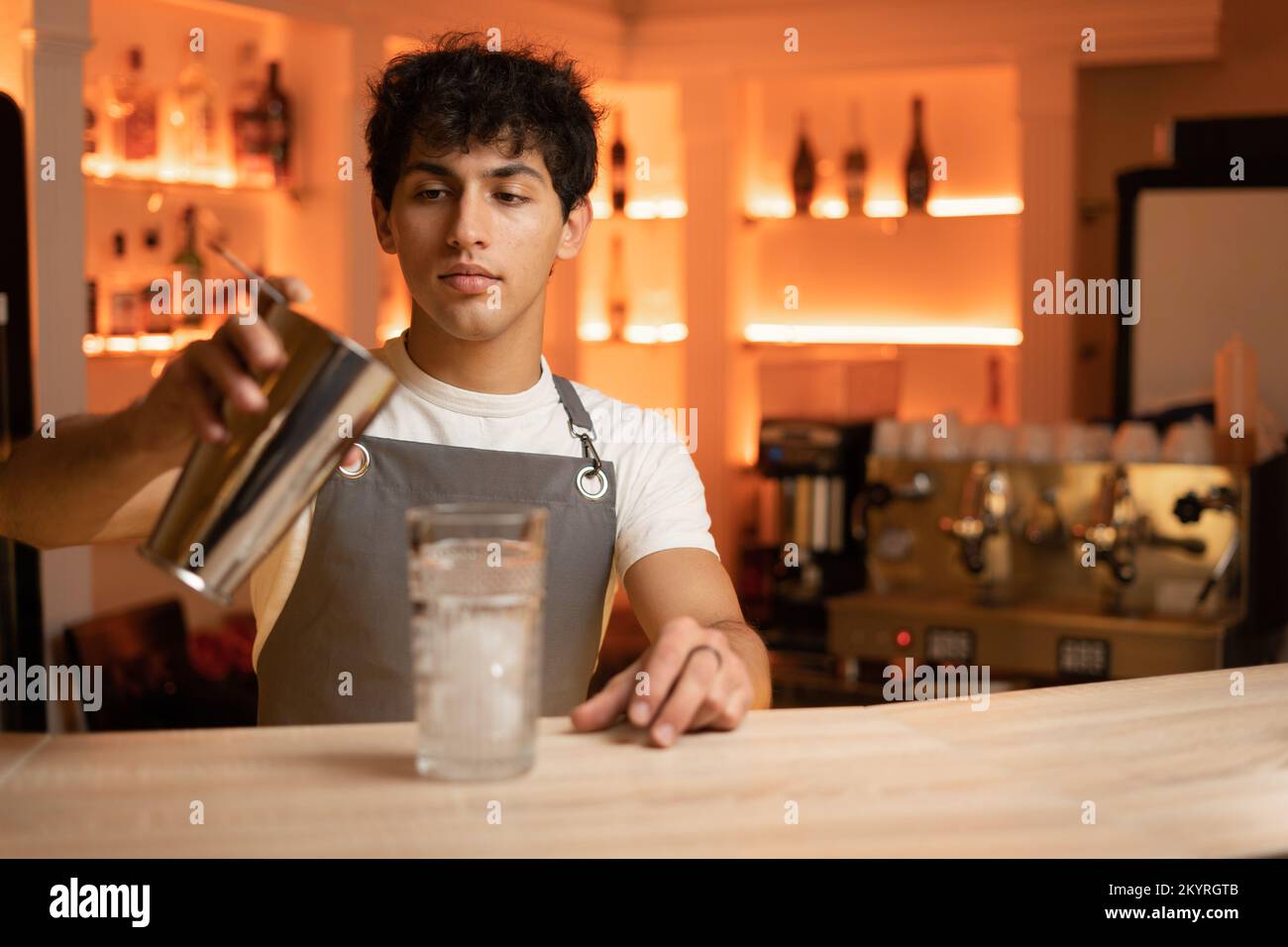Barman is making alcohol cocktail at counter pouring from shaker into ...