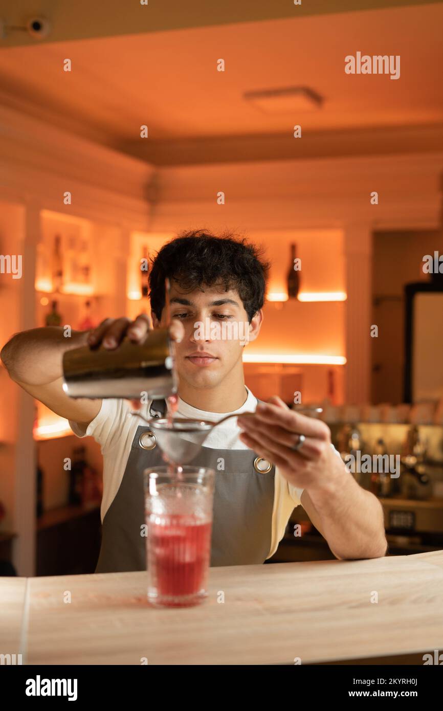 man bartender carefully filters bright alcoholic cocktail from steel ...