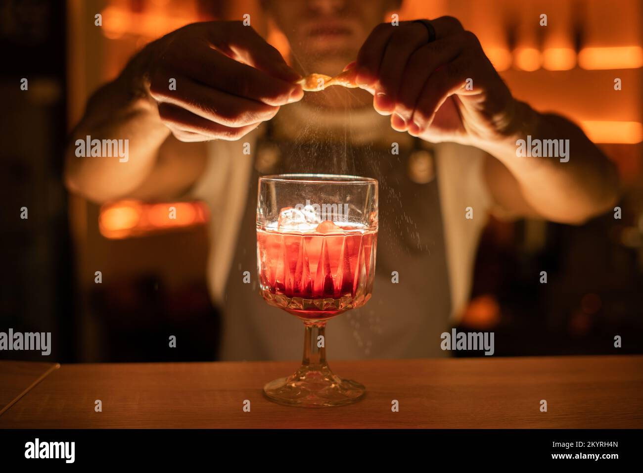 Bartender making a sweet summer cocktail with orange juice on the bar counter, gently sprinkles ...