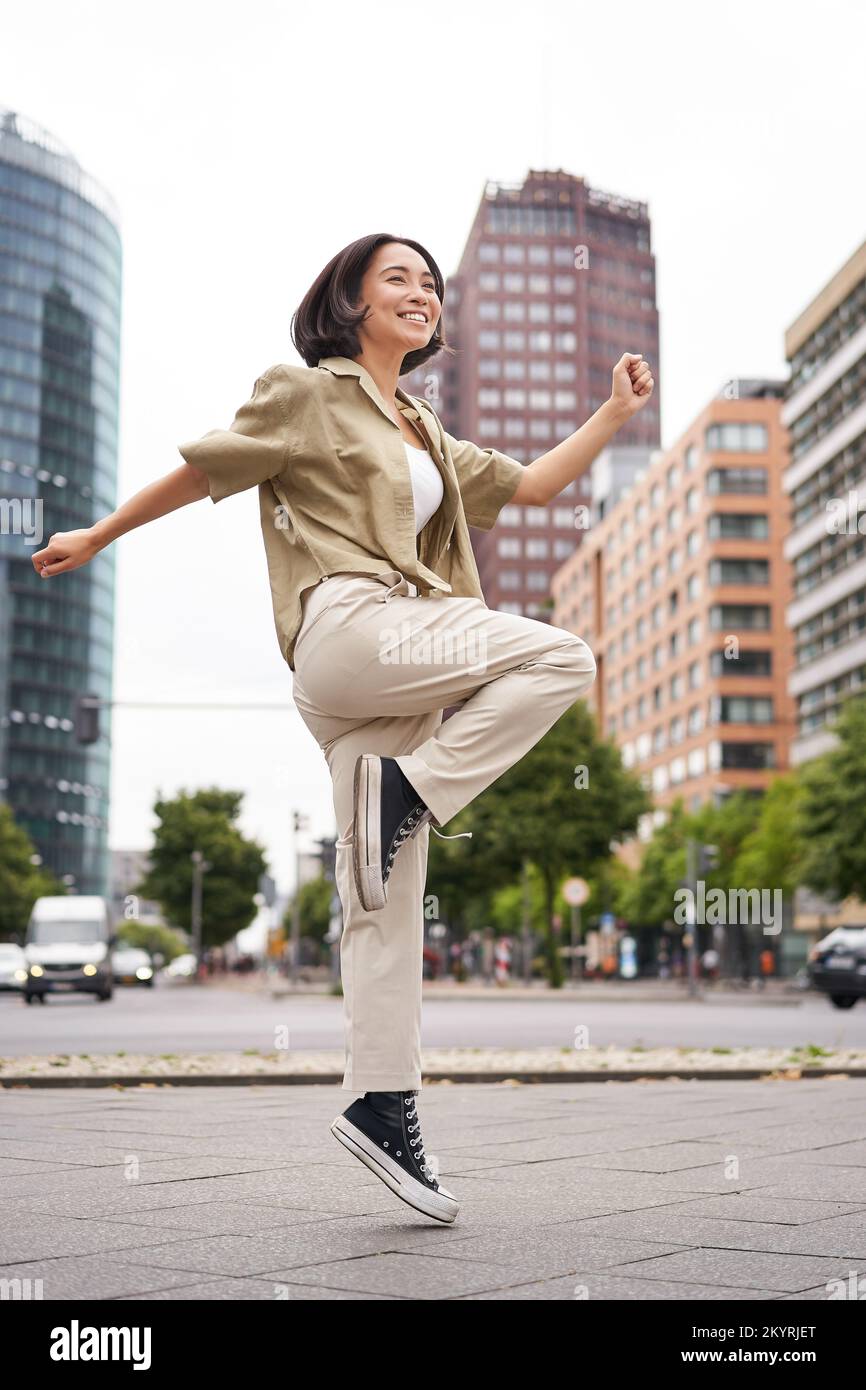 Vertical shot of young asian woman posing happy, raising hands up and ...