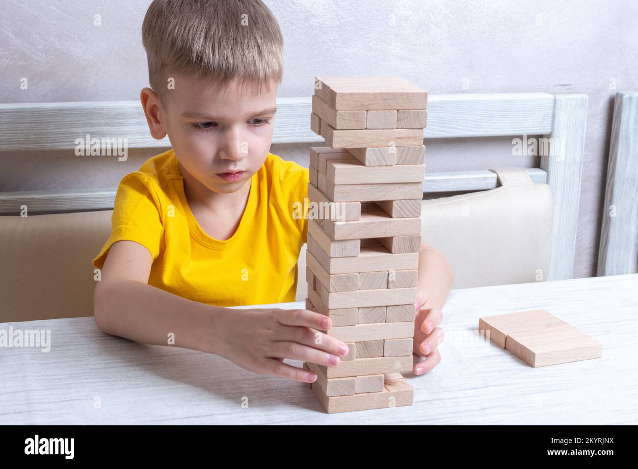 Interested happy little blond boy playing board game taking bricks from ...