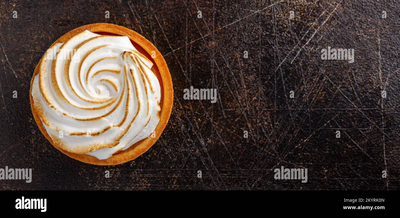 Overhead shot of a small lemon meringue tart on dark rustic background ...