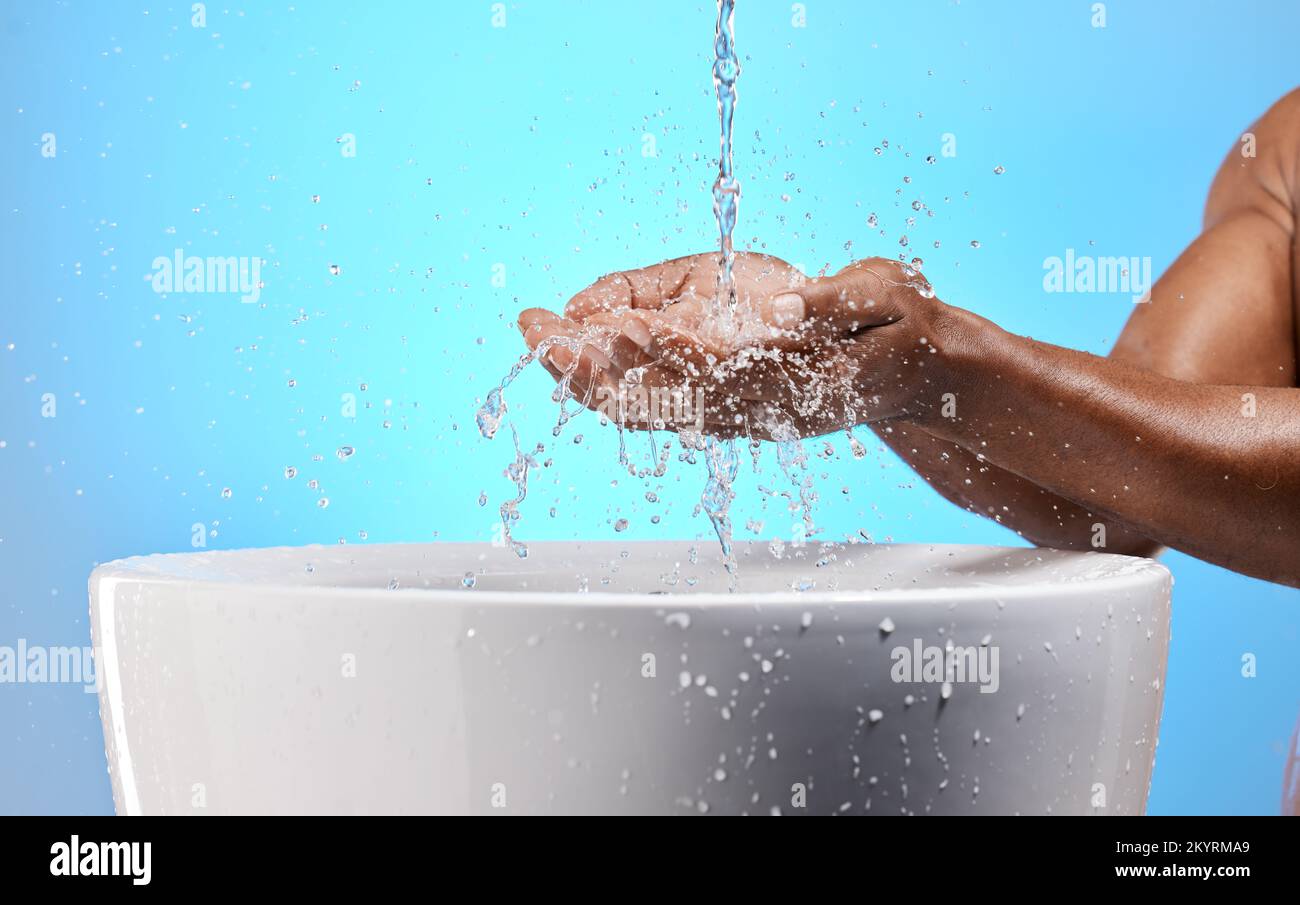 Black man, water splash and washing hands on blue background in studio hygiene maintenance ...