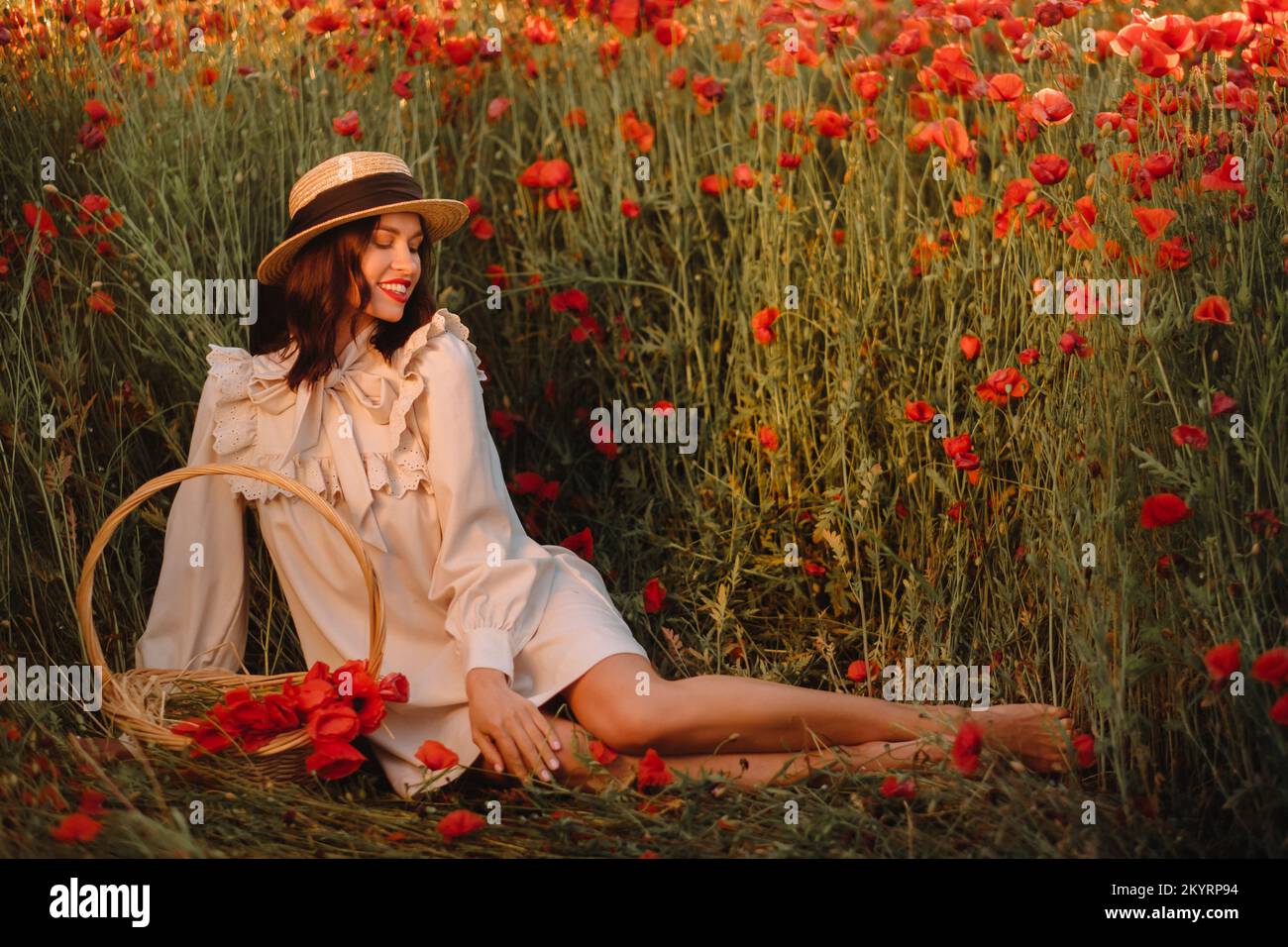A girl in a white dress and with a basket of poppies is sitting on a ...