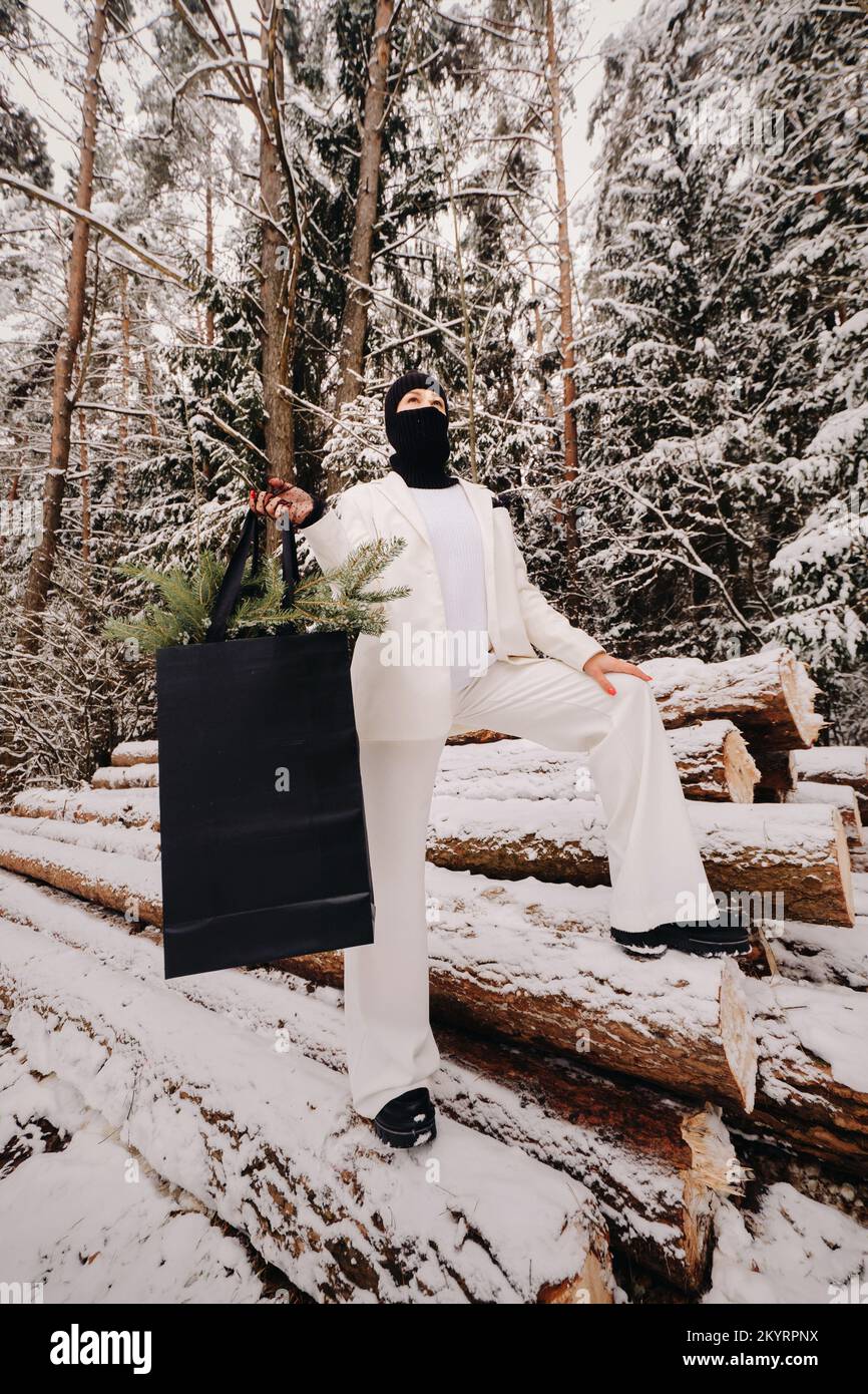 A girl in a white suit and balaclava with a package of Christmas trees ...