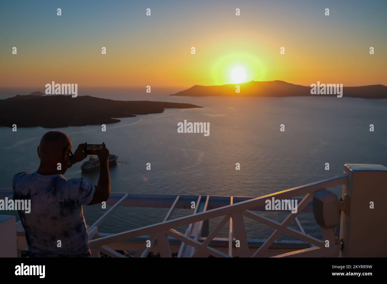 View of a tourist taking a photo of a spectacular golden sunset in Fira ...