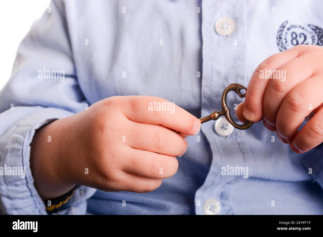 Baby with a blue shirt holding a metal key in his hand on a white ...