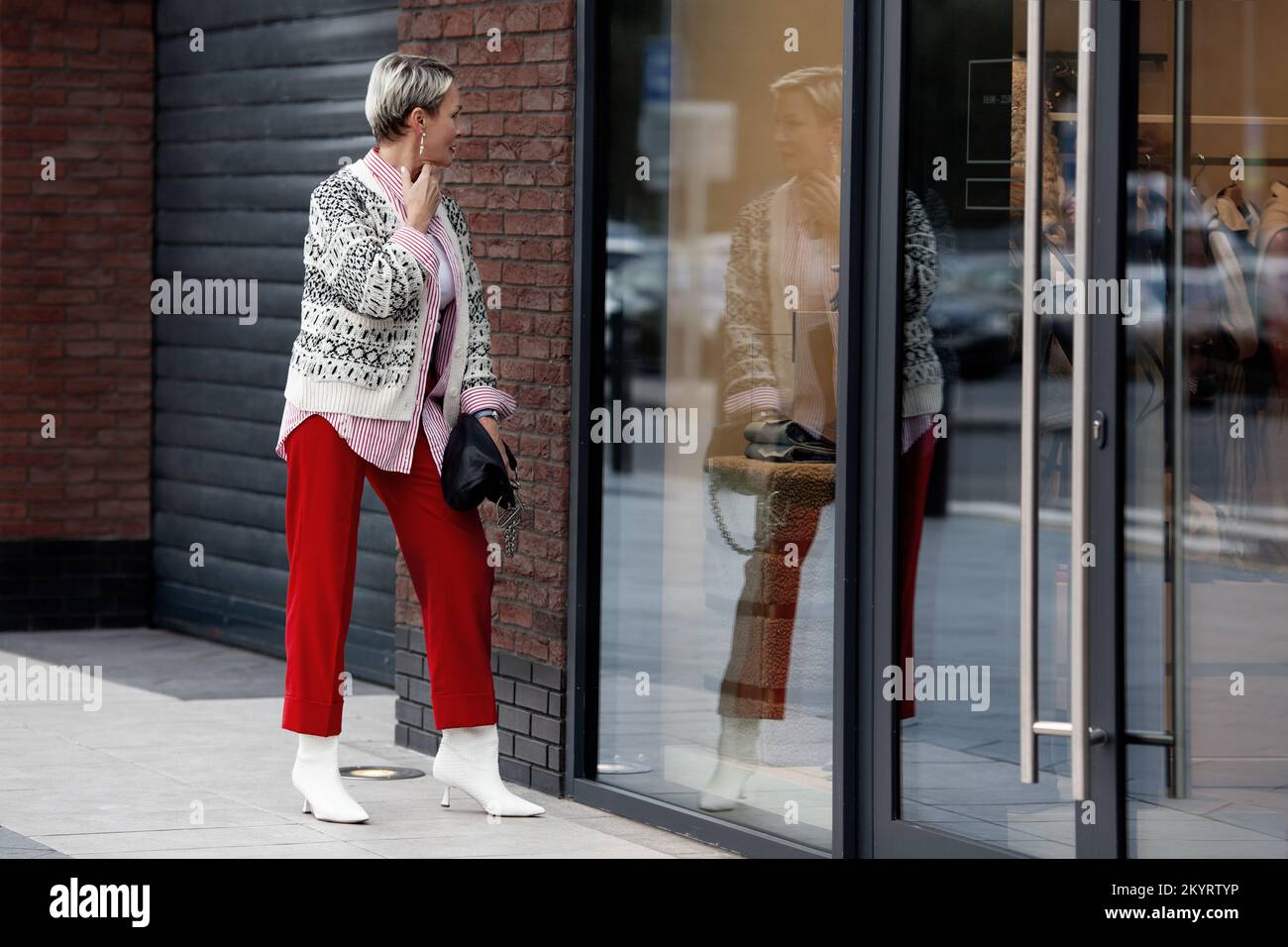 Fashionably dressed woman shopping, looking at reflection in mirror of shop window outside ...