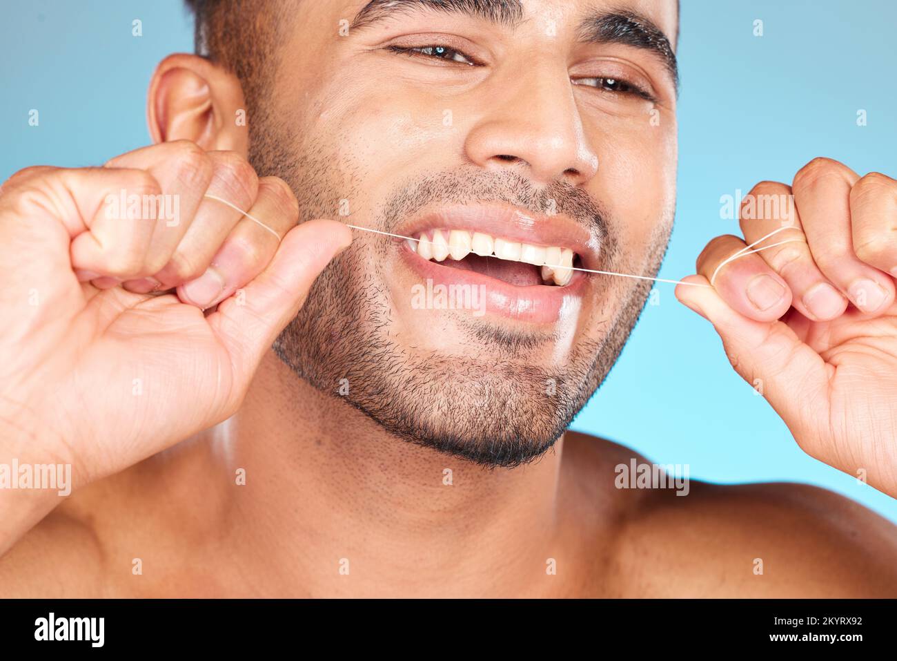 Face, dental and man floss teeth in studio isolated on blue background ...