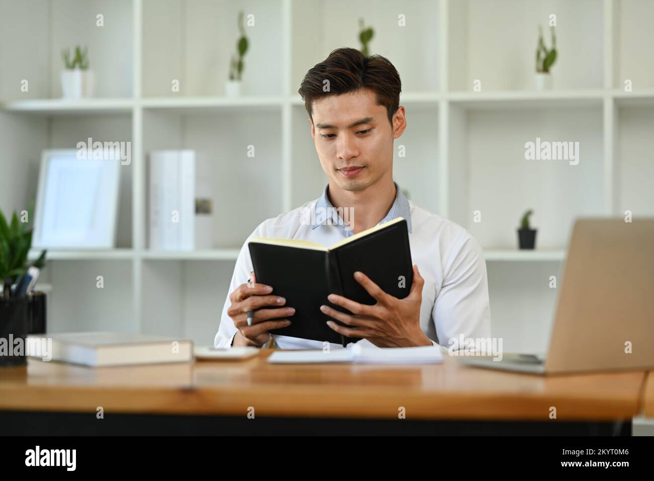 Smart asian male manager analyzing weekly schedule in his notebook ...