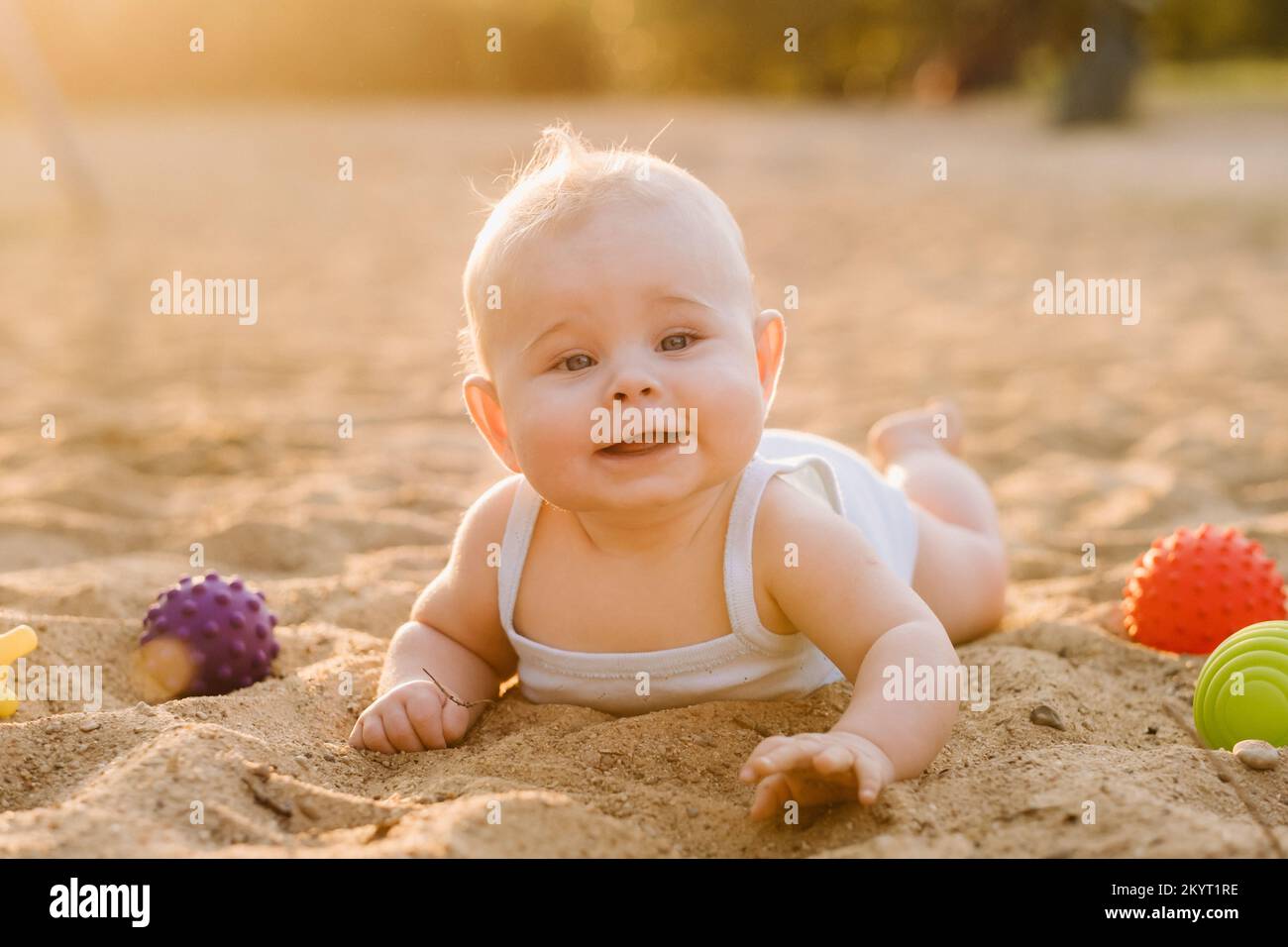 A happy little boy is lying on a sandy beach near the sea in the rays ...