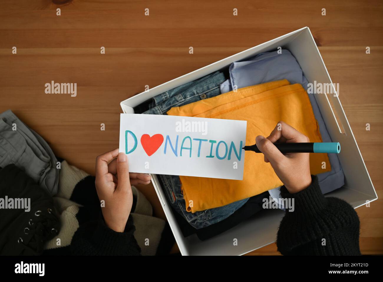 Woman hand writing donation label over box with clothes on wooden table ...