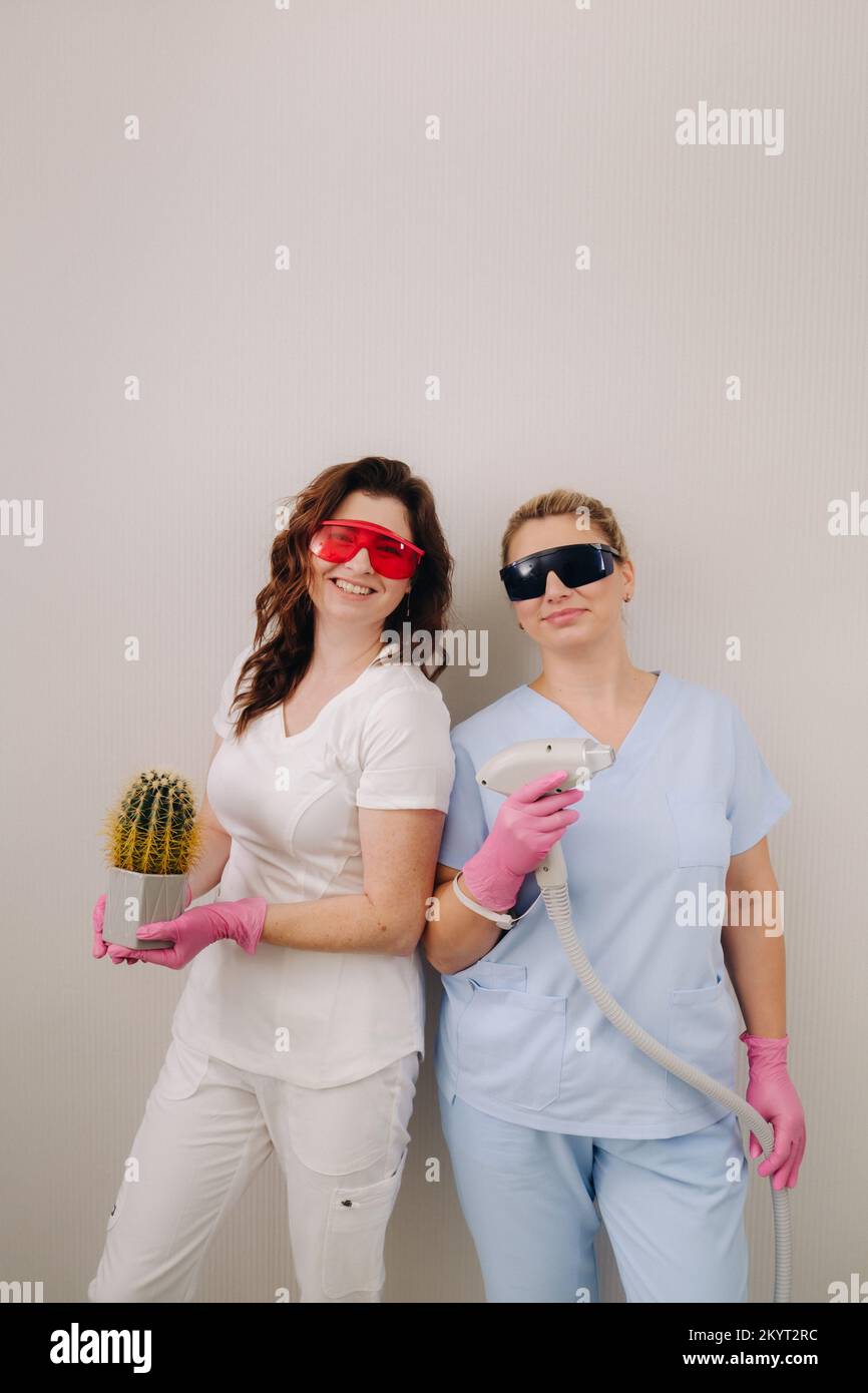 Two cosmetologists in protective glasses are holding a laser depilation ...