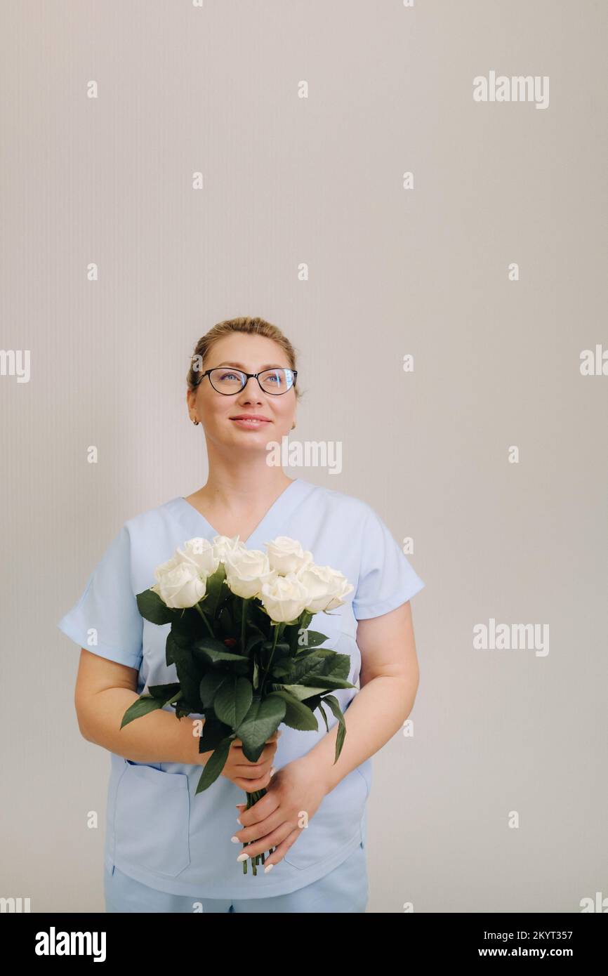 A female doctor in a blue robe with a bouquet of white roses in her ...