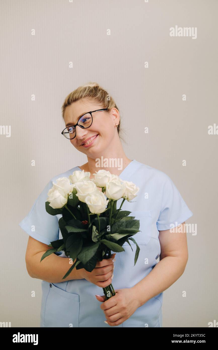 A female doctor in a blue robe with a bouquet of white roses in her ...