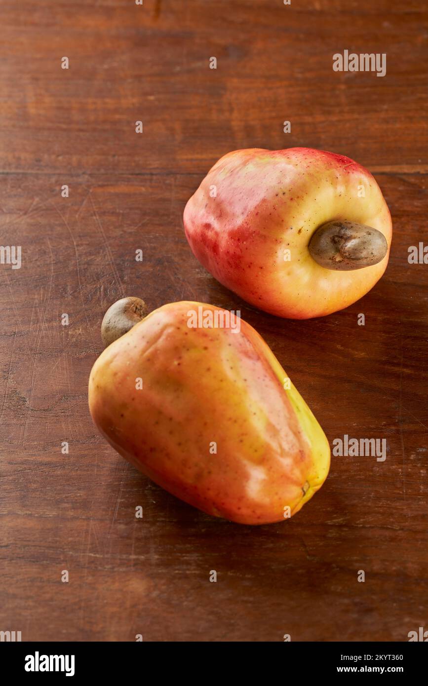 two cashew nut fruits on a wooden table with focus on the back one ...