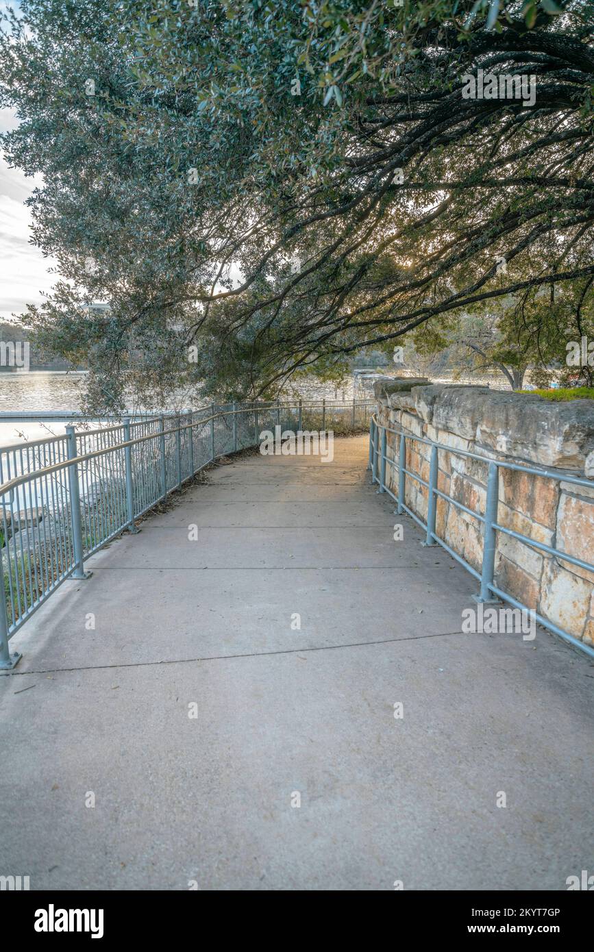 Paved pathway in Austin Texas along a river and under a canopy of trees ...