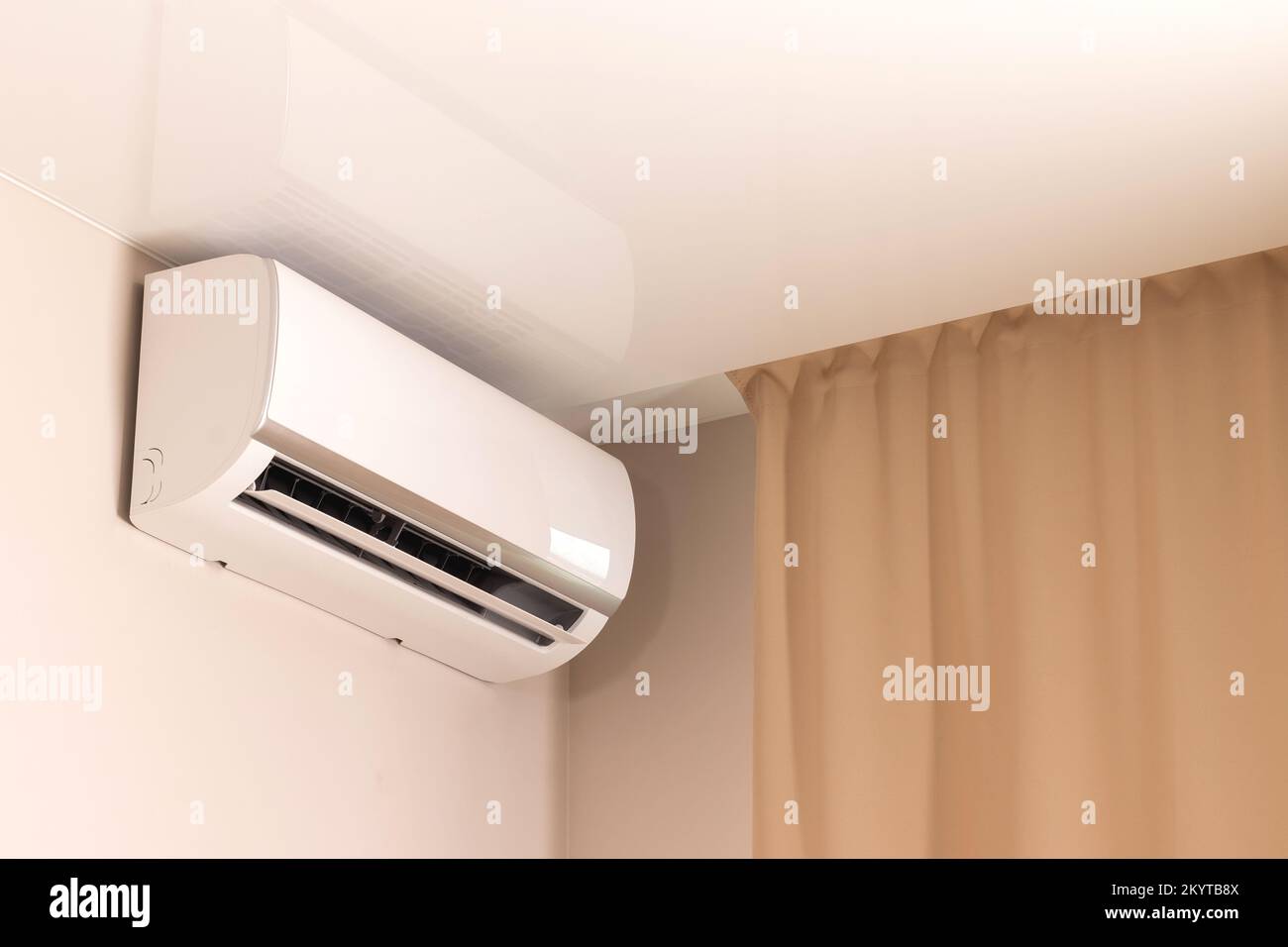 White air conditioner under stretch ceiling in modern room with beige curtains Stock Photo - Alamy