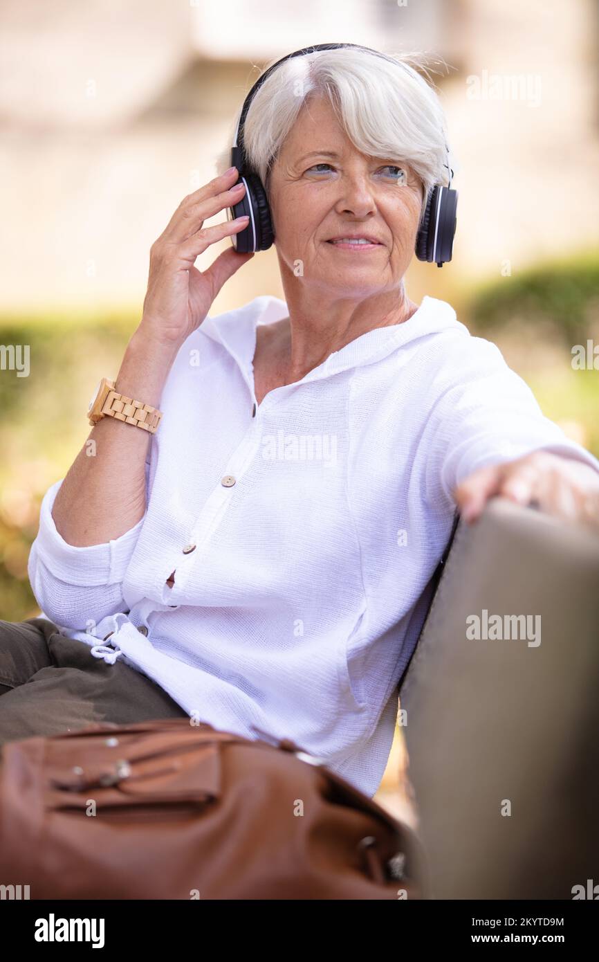 senior woman wearing wireless headphones on the bench Stock Photo - Alamy