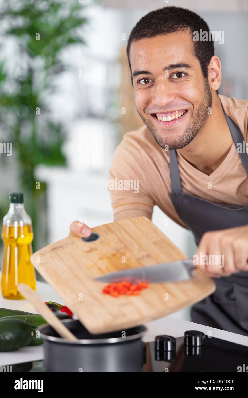 young man smiling as he slides vegetables into pan Stock Photo - Alamy