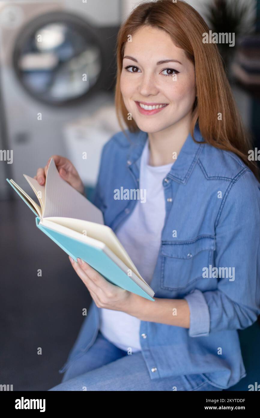 beautiful young woman reading book at laundromat Stock Photo - Alamy
