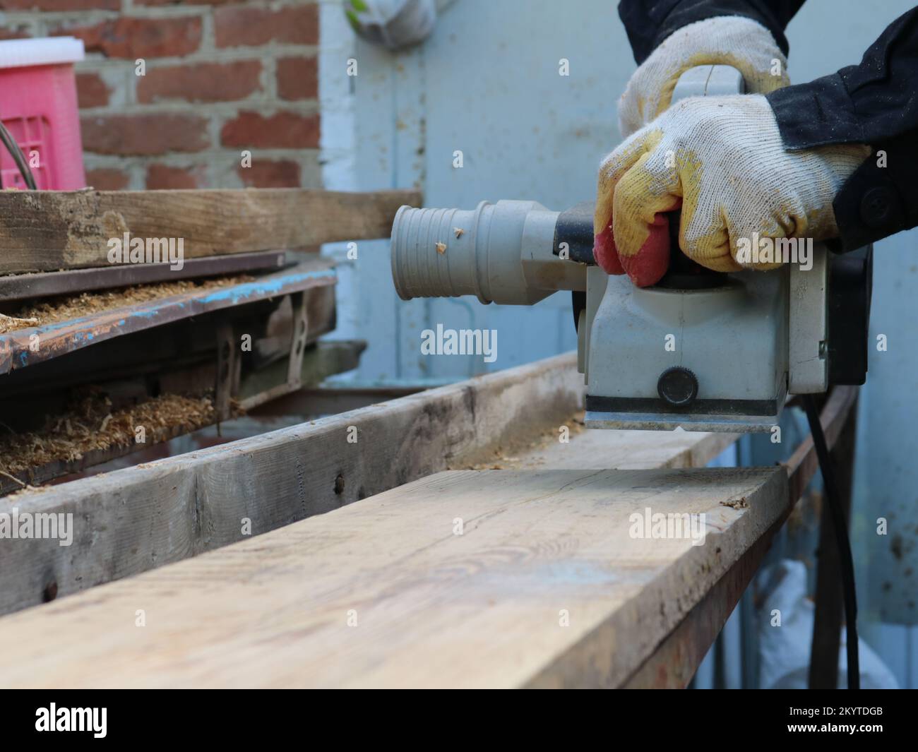 electric planer in the glove hands of a carpenter, working with wood ...