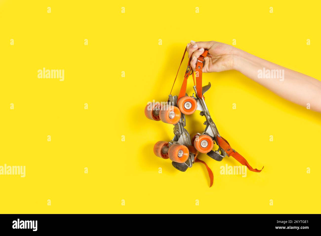 Woman hand holding a pair of metal roller skates on a yellow background ...