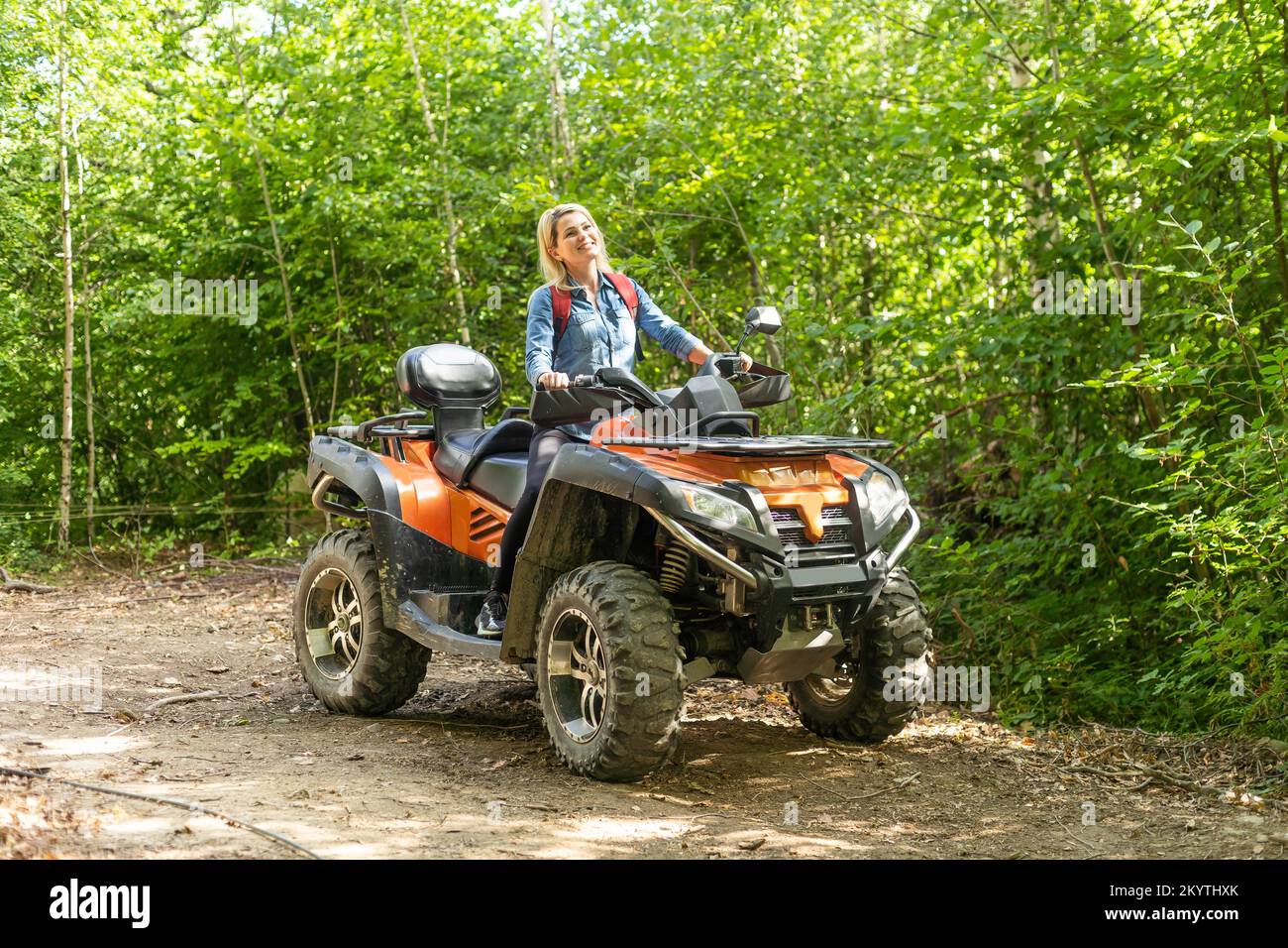 Smiling happy woman riding quad bike on a sunny day, against blue sky. Low angle shot. Freedom ...