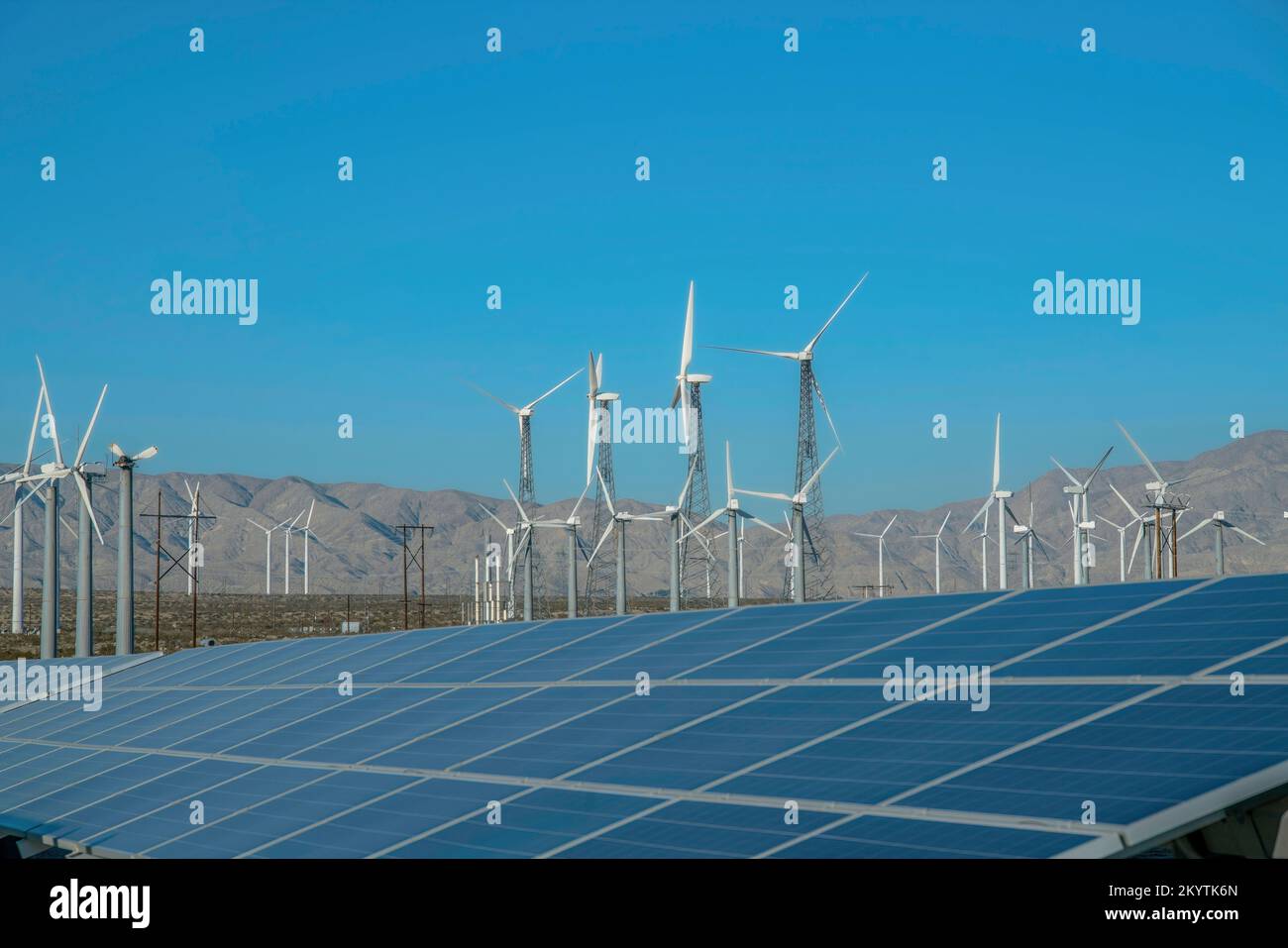Windmills and solar panels against mountain and blue sky background ...