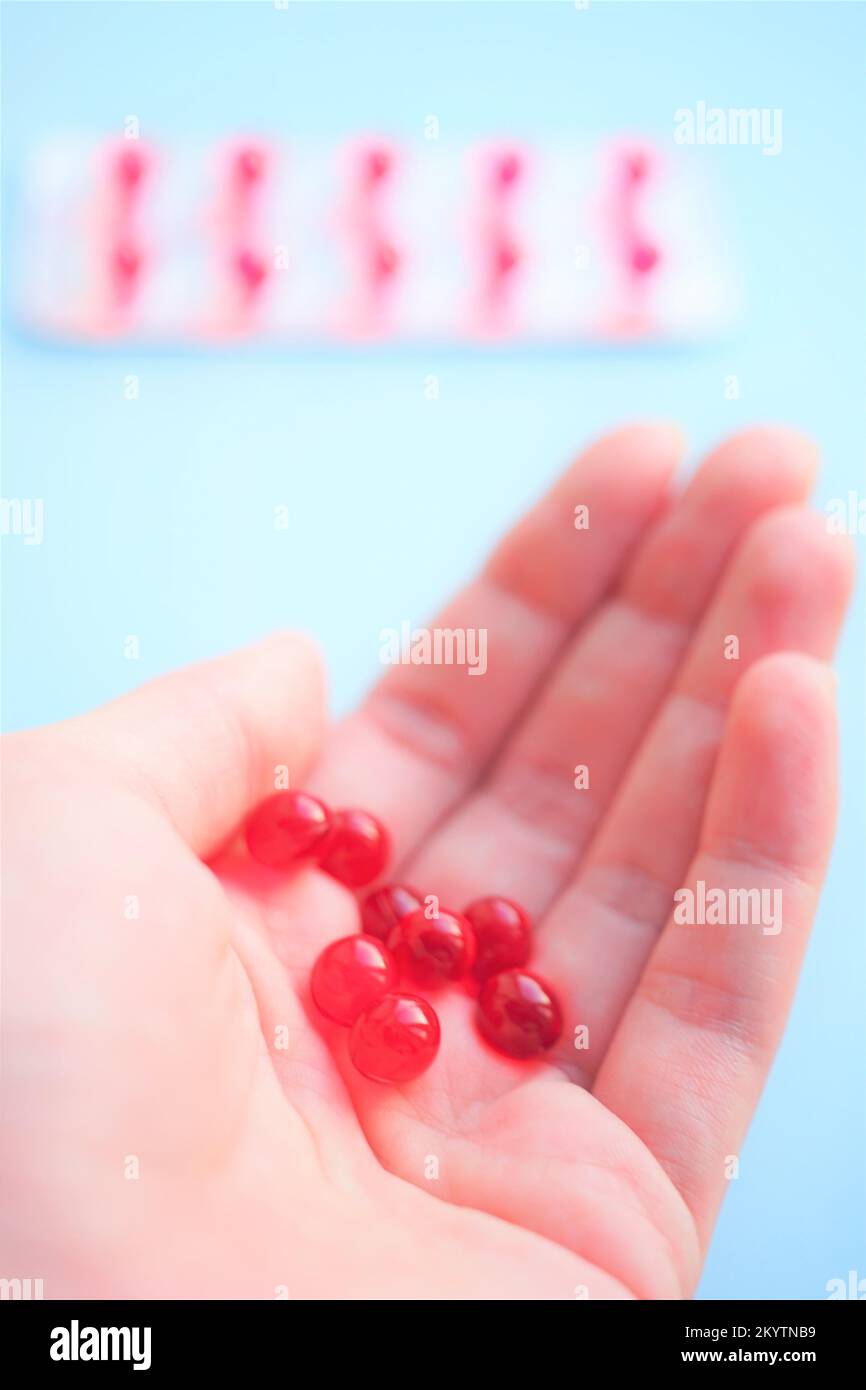 Round red vitamins in human palm. Pale blue background Stock Photo - Alamy