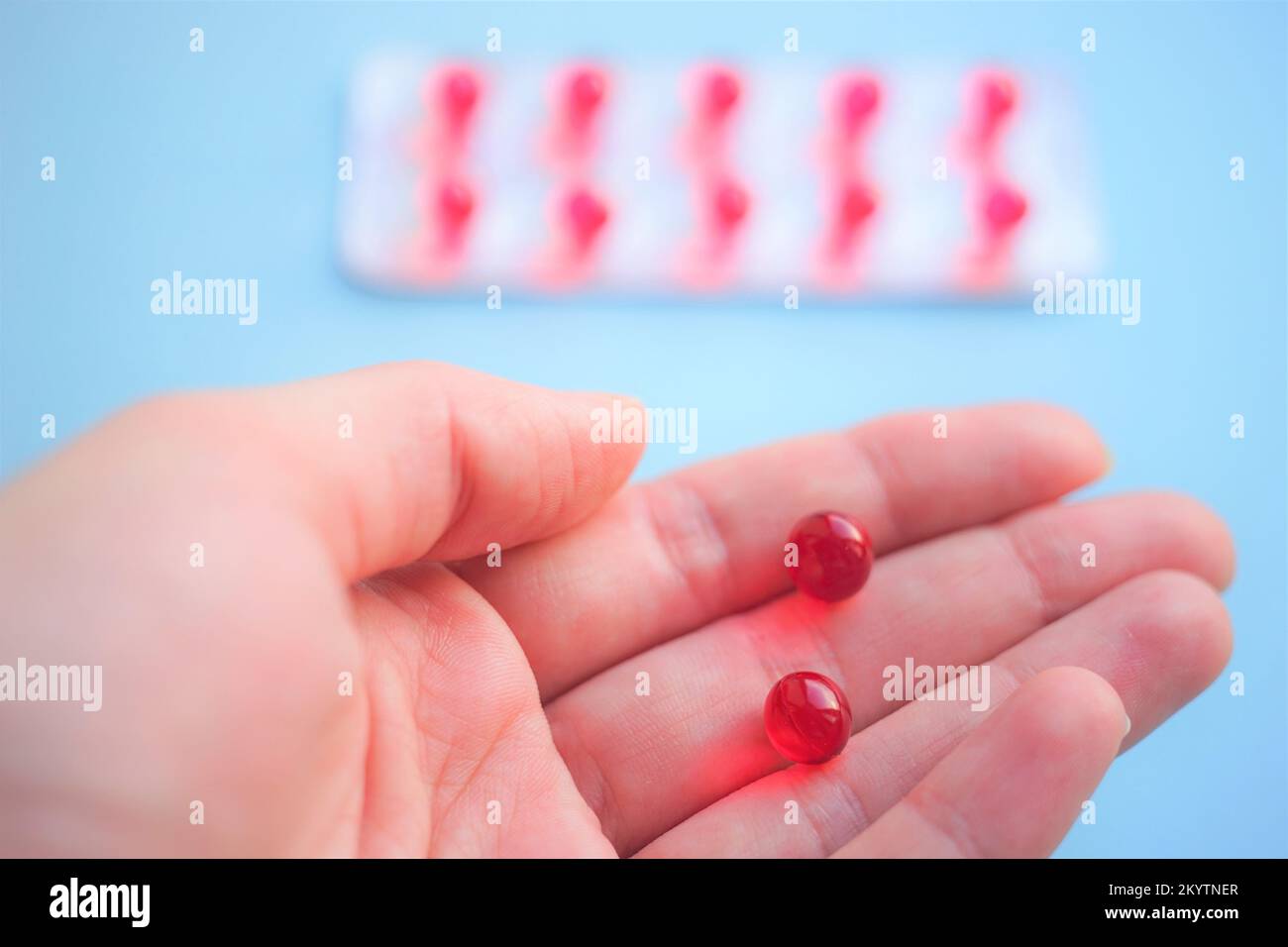 Round red vitamins in human palm on pale blue background Stock Photo ...