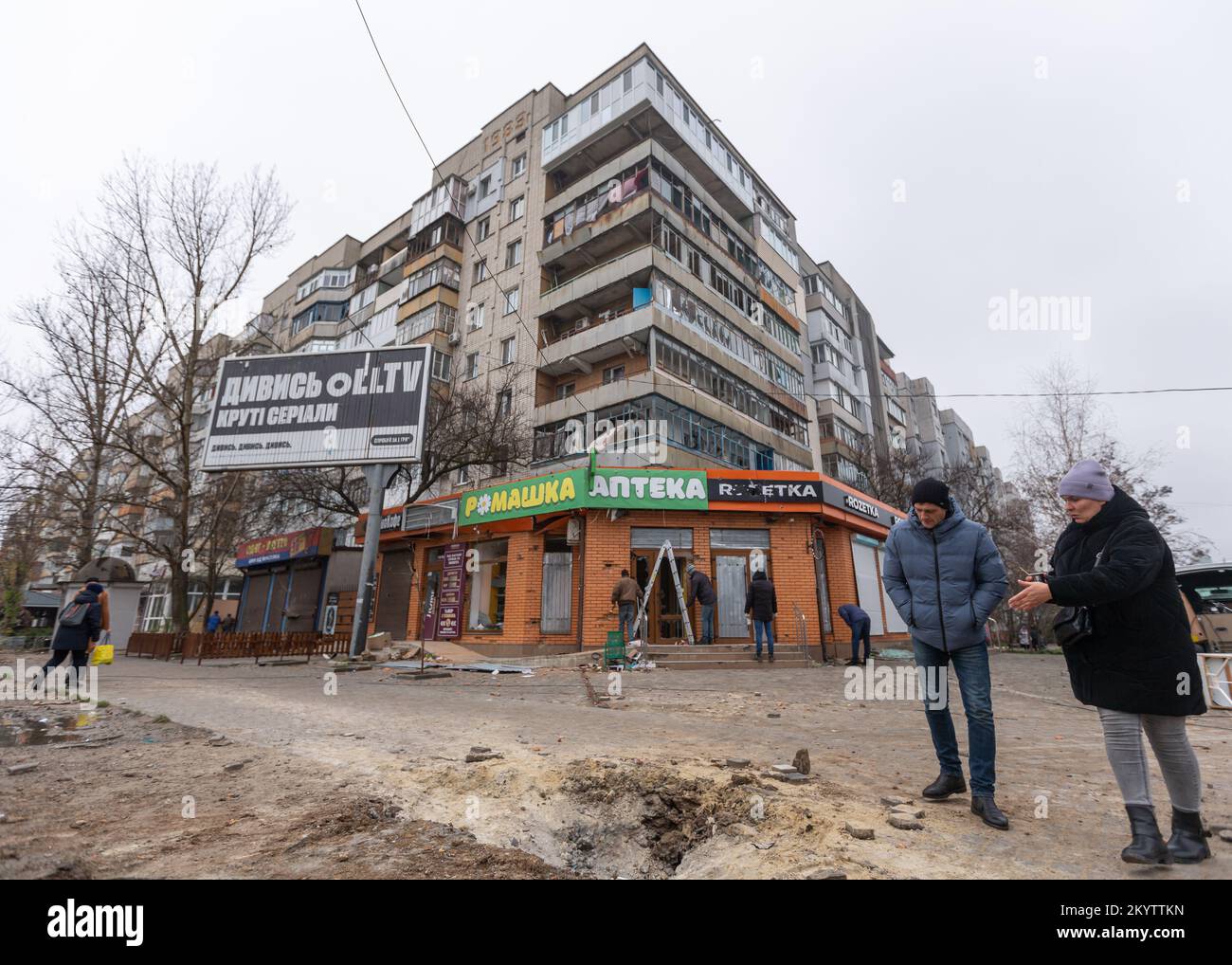 Ukrainian civilians point and look at a shell hole in the sidewalk ...