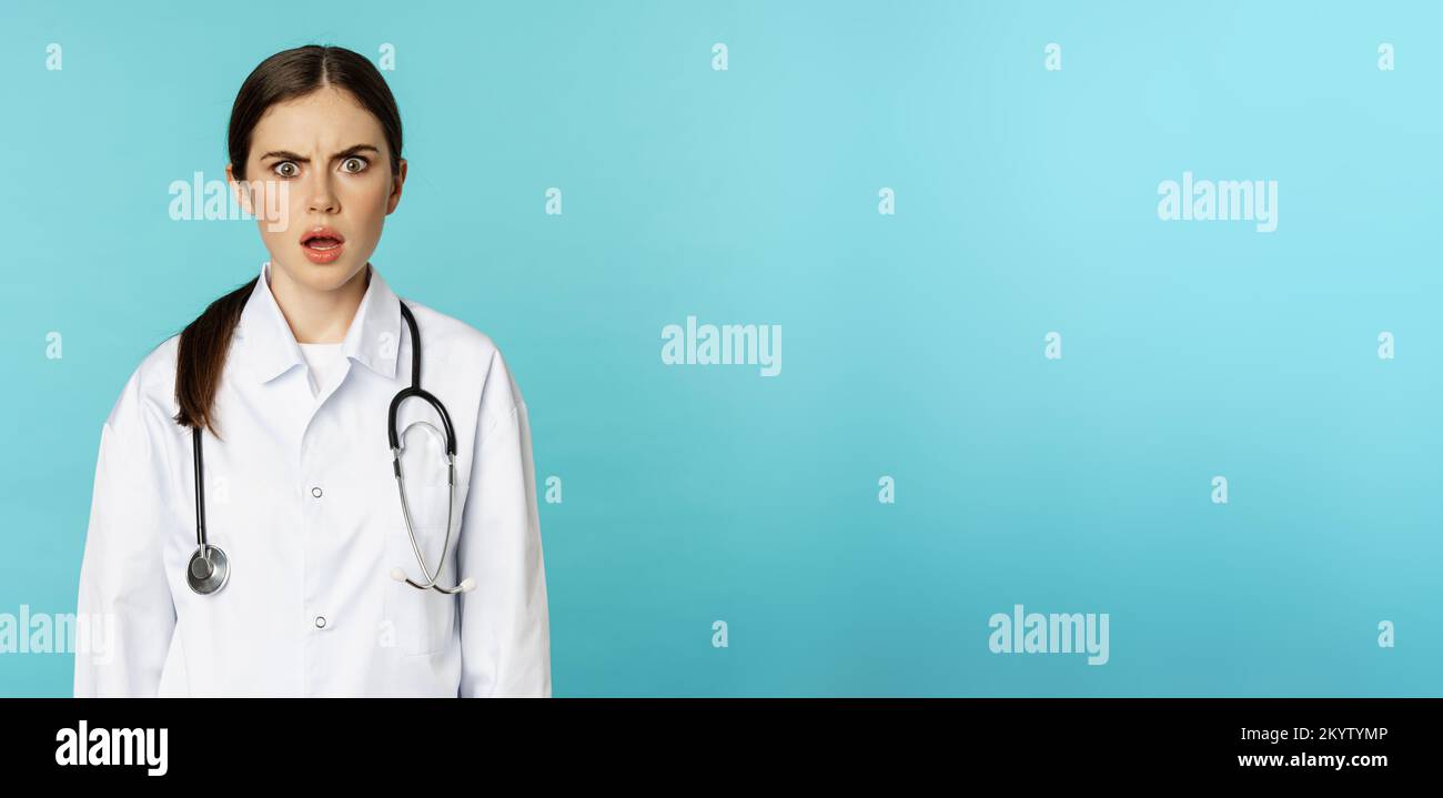 Portrait of shocked woman doctor, female hospital intern in white coat ...