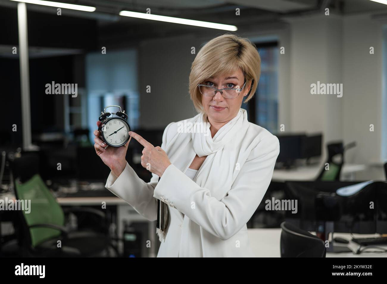Caucasian business woman showing on alarm clock in office Stock Photo ...
